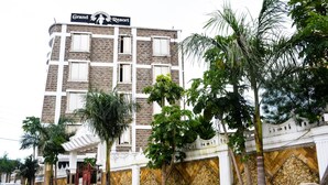 Um hotel com uma placa que diz "Grand Resort", apresentando fachada de tijolos, grades brancas e palmeiras.