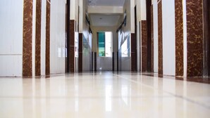 Um corredor longo e bem cuidado, com colunas de mármore e piso brilhante, que leva a um quarto claro com janela.