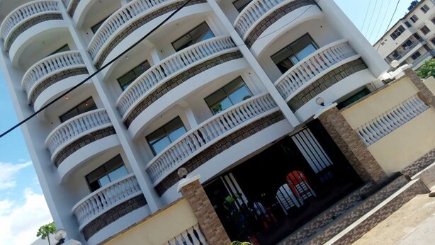 Um edifício com várias andares, varandas, entrada de garagem e céu claro.