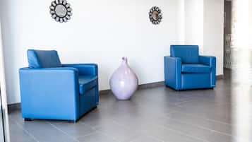 Um hall moderno com duas poltronas azuis, um vaso grande e espelhos decorativos nas paredes.