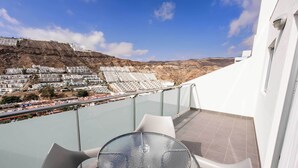 Uma varanda com mesa e cadeiras de vidro, com vista para uma encosta com edifícios.
