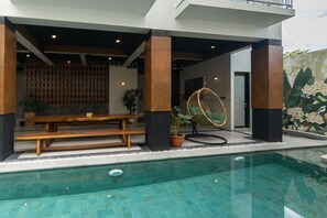 Área da piscina com uma cadeira suspensa, um banco de madeira e um vaso com planta.