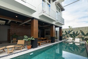 Uma área de piscina moderna ao ar livre, com espreguiçadeiras, um banco de madeira e plantas em vasos.