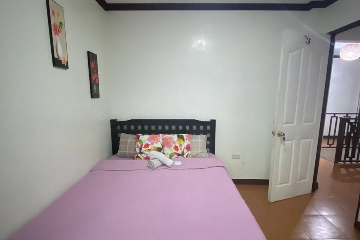 Quarto com uma cama, uma porta e uma parede com duas imagens.