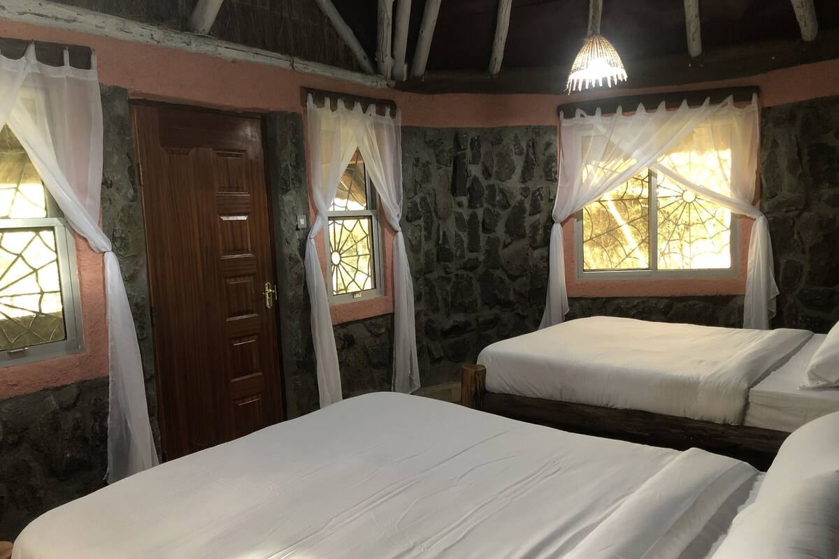 Um quarto rústico com duas camas, paredes de pedra, vigas de madeira e uma porta de madeira.