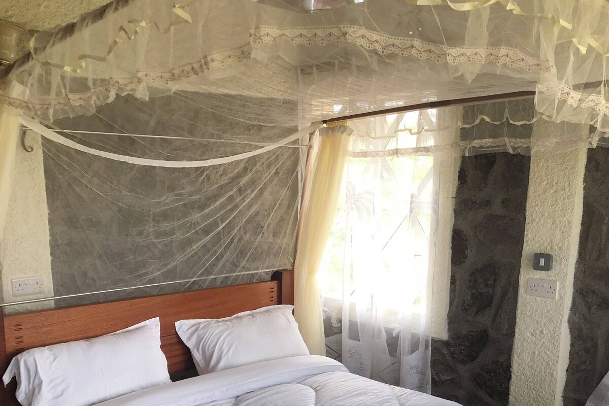 Uma cama com estrutura de madeira, roupa de cama branca e mosquiteiro sobre a cama.