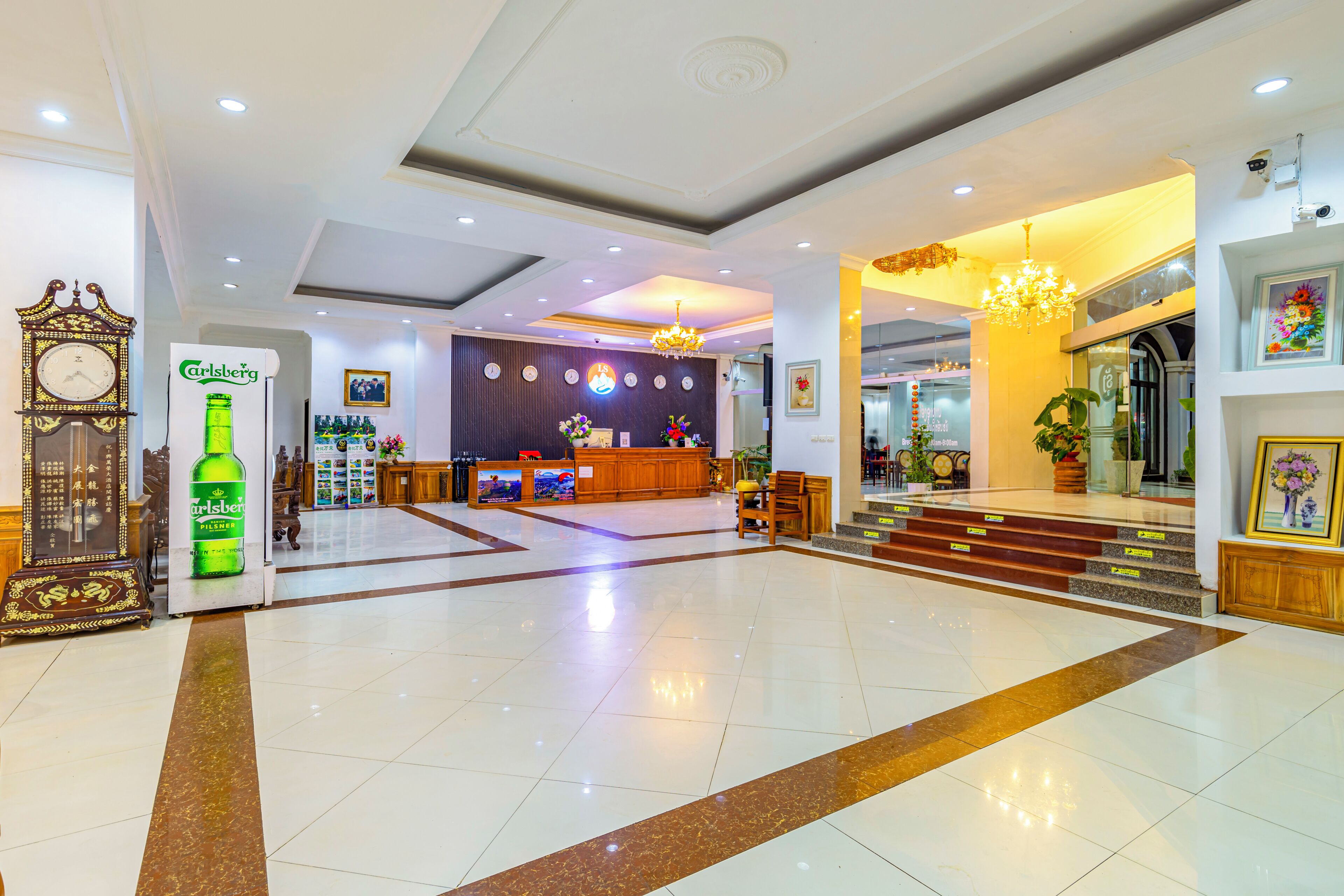 Um saguão de hotel com uma mesa de recepção, um relógio e uma grande garrafa verde de Carlsberg.