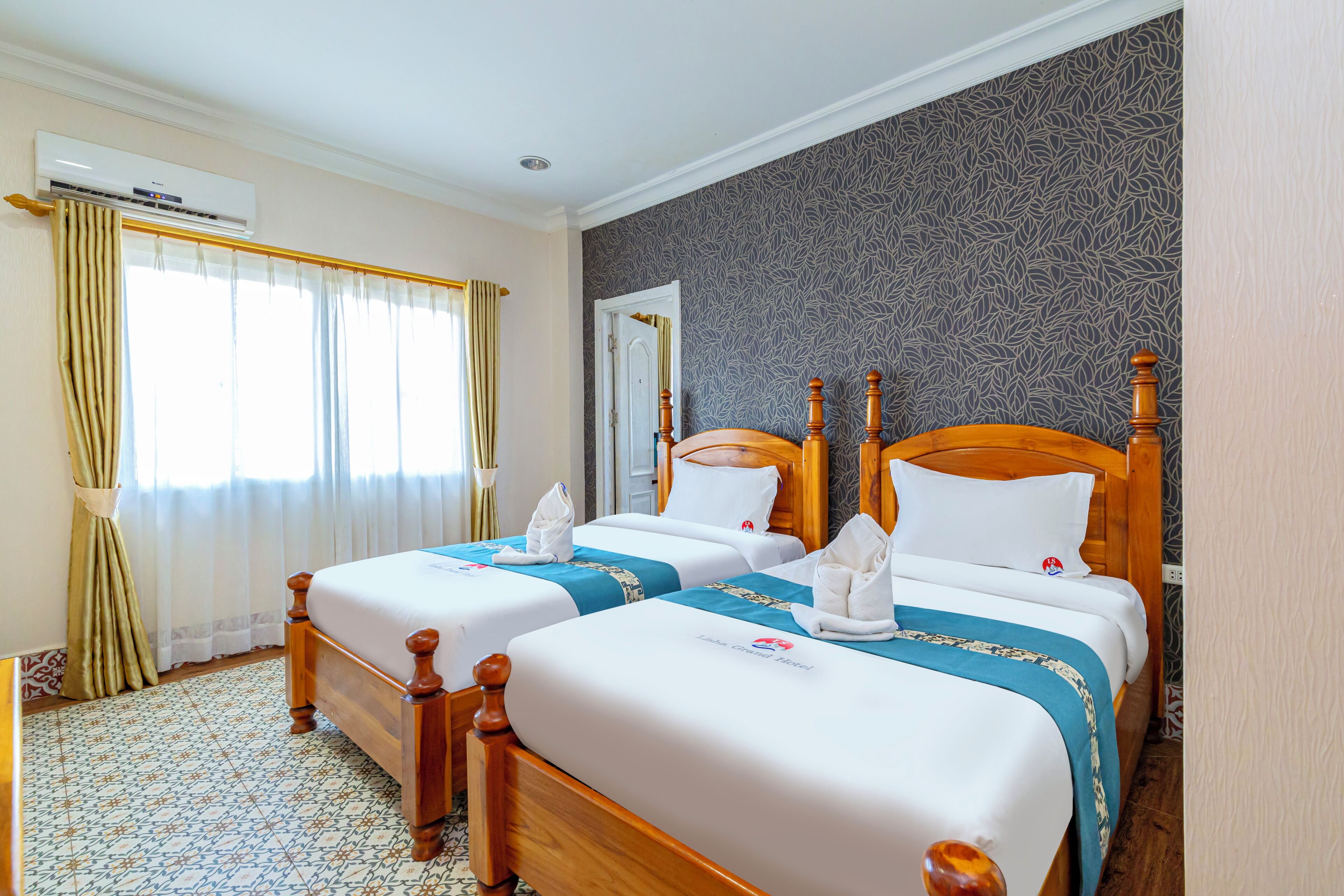 Quarto de hotel com duas camas de madeira, um papel de parede estampado e uma janela com cortinas.