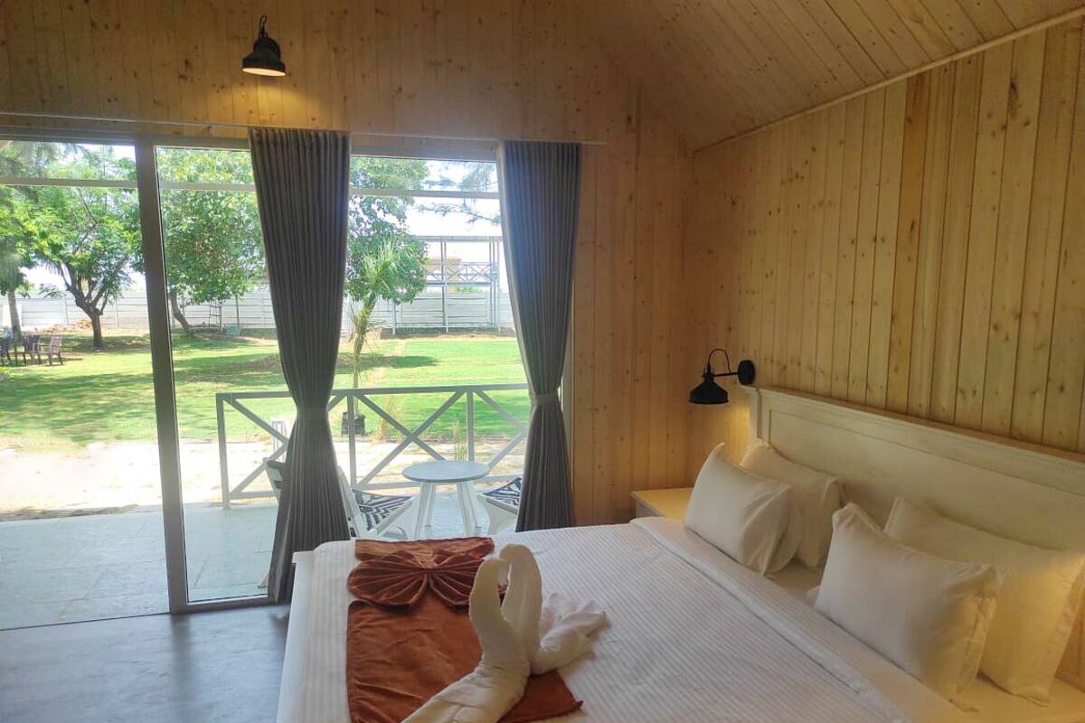 Quarto de madeira com uma cama, uma mesa e vista para uma área gramada lá fora.
