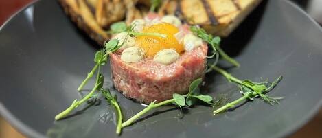 Um prato de tatare de carne com gema de ovo crua, decorado com ervas, servido em um prato escuro.