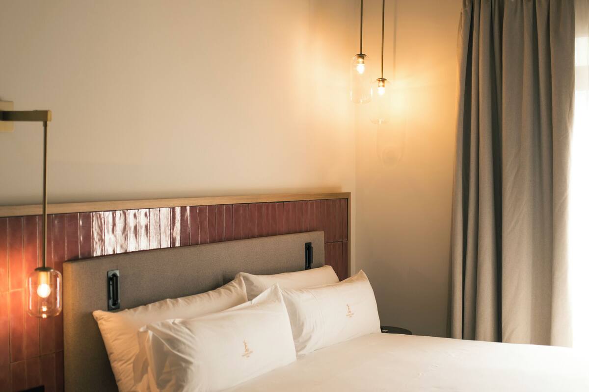 Quarto de hotel com cama grande, cabeceira de madeira e iluminação pendente.