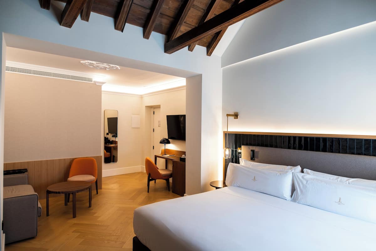 Quarto de hotel com uma cama grande, uma escrivaninha, uma cadeira e uma televisão.