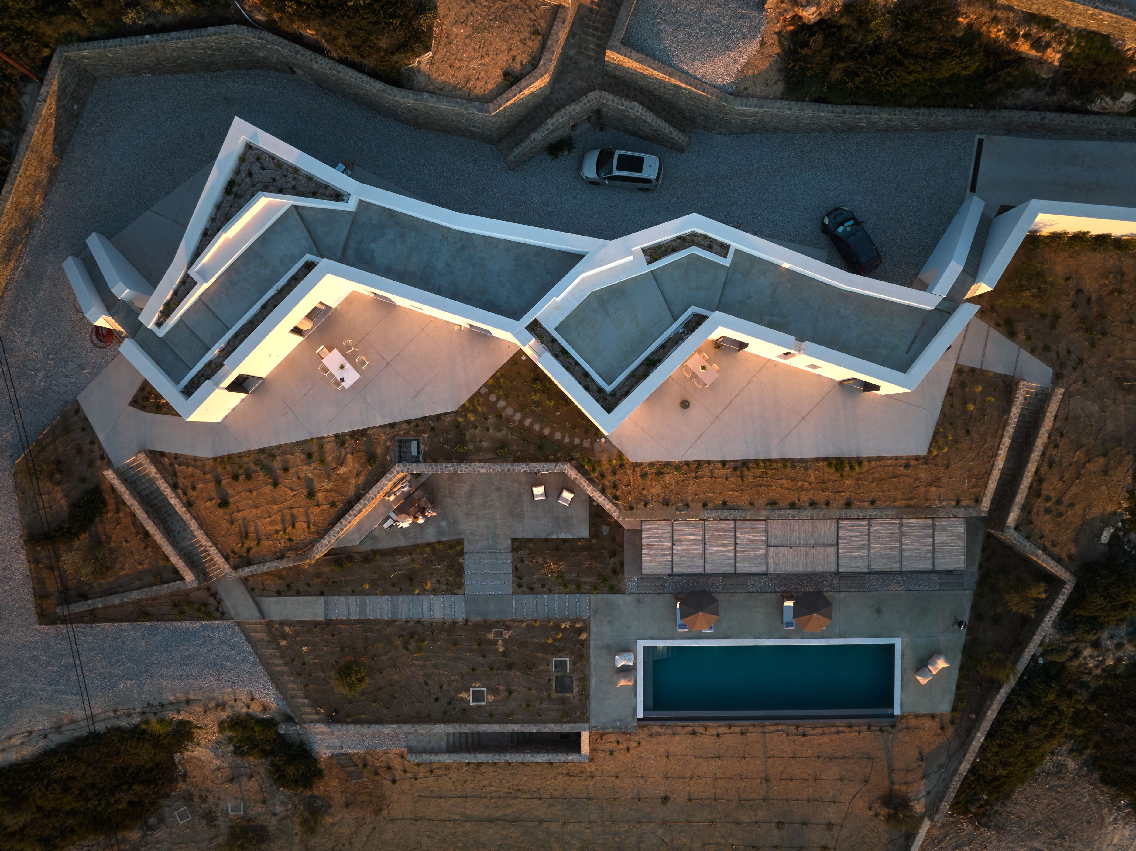 Vista aérea de uma casa moderna com piscina, área de estar externa e entrada de automóveis.