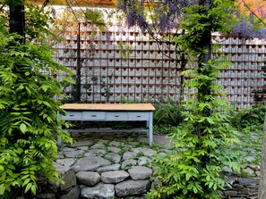 Um banco de pedra num jardim com uma vedação de metal e plantas em vasos.