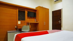 Quarto de hotel com uma cama, uma escrivaninha, uma cadeira, uma televisão e um guarda-roupa.