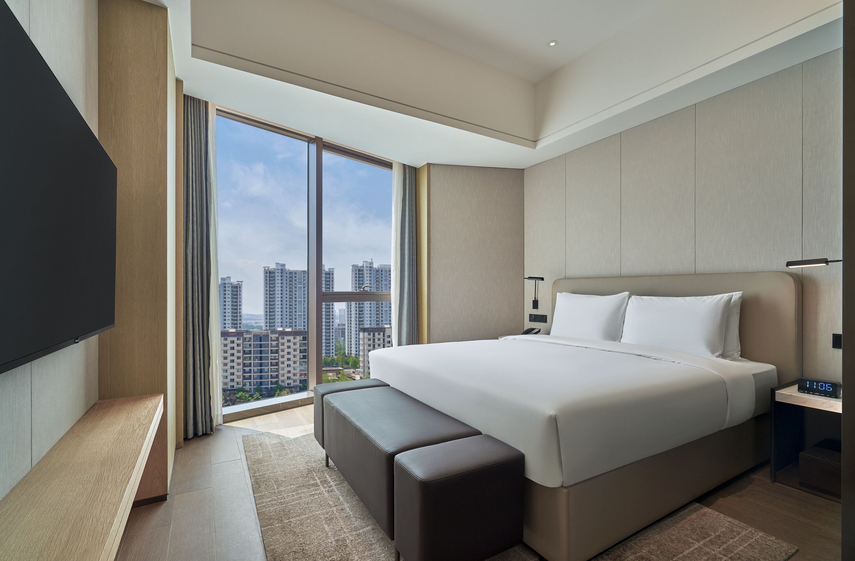 Quarto de hotel moderno com uma cama grande, televisão de tela plana e vista para a cidade.