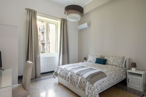 Quarto com cama, cadeira, mesa de cabeceira e janela com cortinas.