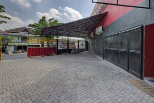 Um pátio pavimentado com área coberta, um portão vermelho e um edifício com uma grande porta de garagem.