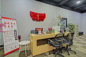 Bancada de recepção com duas cadeiras de escritório pretas, uma pequena mesa branca, uma placa vermelha e branca e um mural com cartazes informativos.