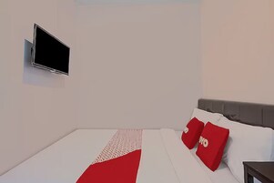 Quarto de hotel moderno com cama, televisão de tela plana na parede e almofadas vermelhas e brancas.