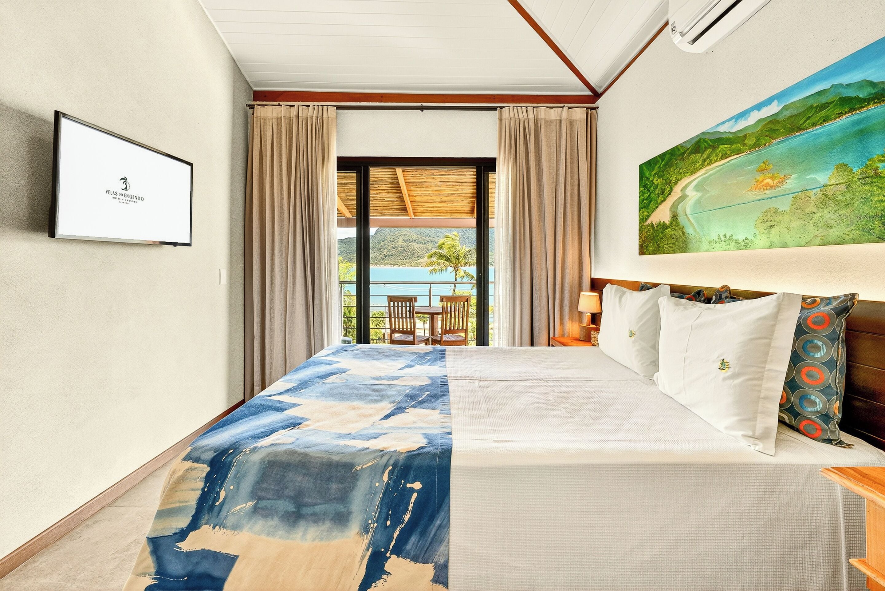 Quarto de hotel com uma cama, um quadro de uma praia, uma televisão e vista para o exterior.