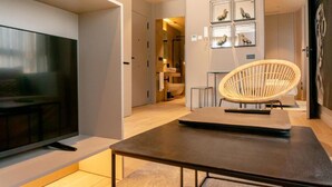 Uma sala de estar moderna com televisão de tela plana, uma mesa de madeira escura e uma cadeira de vime.