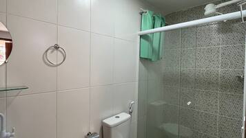Casa de banho com sanita, cabine de duche em vidro e suporte para papel higiénico.