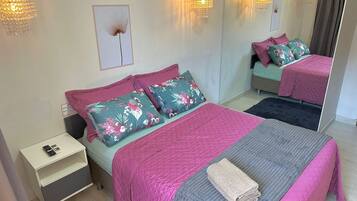 Quarto moderno com cama, mesas de cabeceira, espelho e almofadas decorativas.
