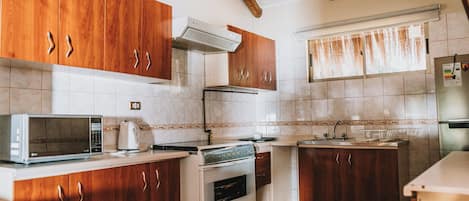 Cozinha com armários de madeira, micro-ondas, forno e janela com cortinas.