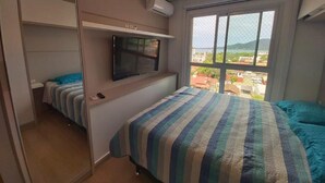Quarto com cama, televisão e janela com vista para a cidade.