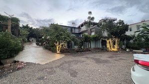 Zona residencial com entrada de automóvel em cascalho, casas com varandas e um carro branco estacionado à direita.