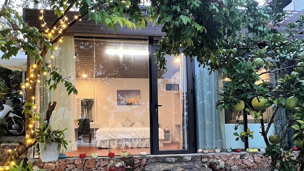 Quarto moderno com cama, cadeira e mesa. Há plantas em vasos do lado de fora da janela.