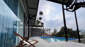 Terraço no telhado com piscina, uma cadeira de madeira e parede de vidro.