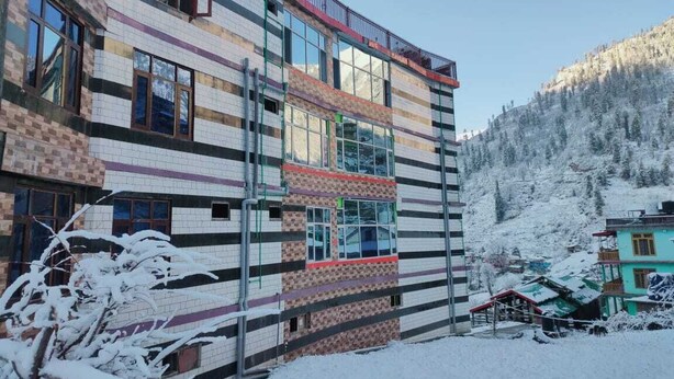 Um edifício de vários andares com fachada de tijolos e vidro, varandas e uma vista clara de uma paisagem montanhosa coberta de neve.