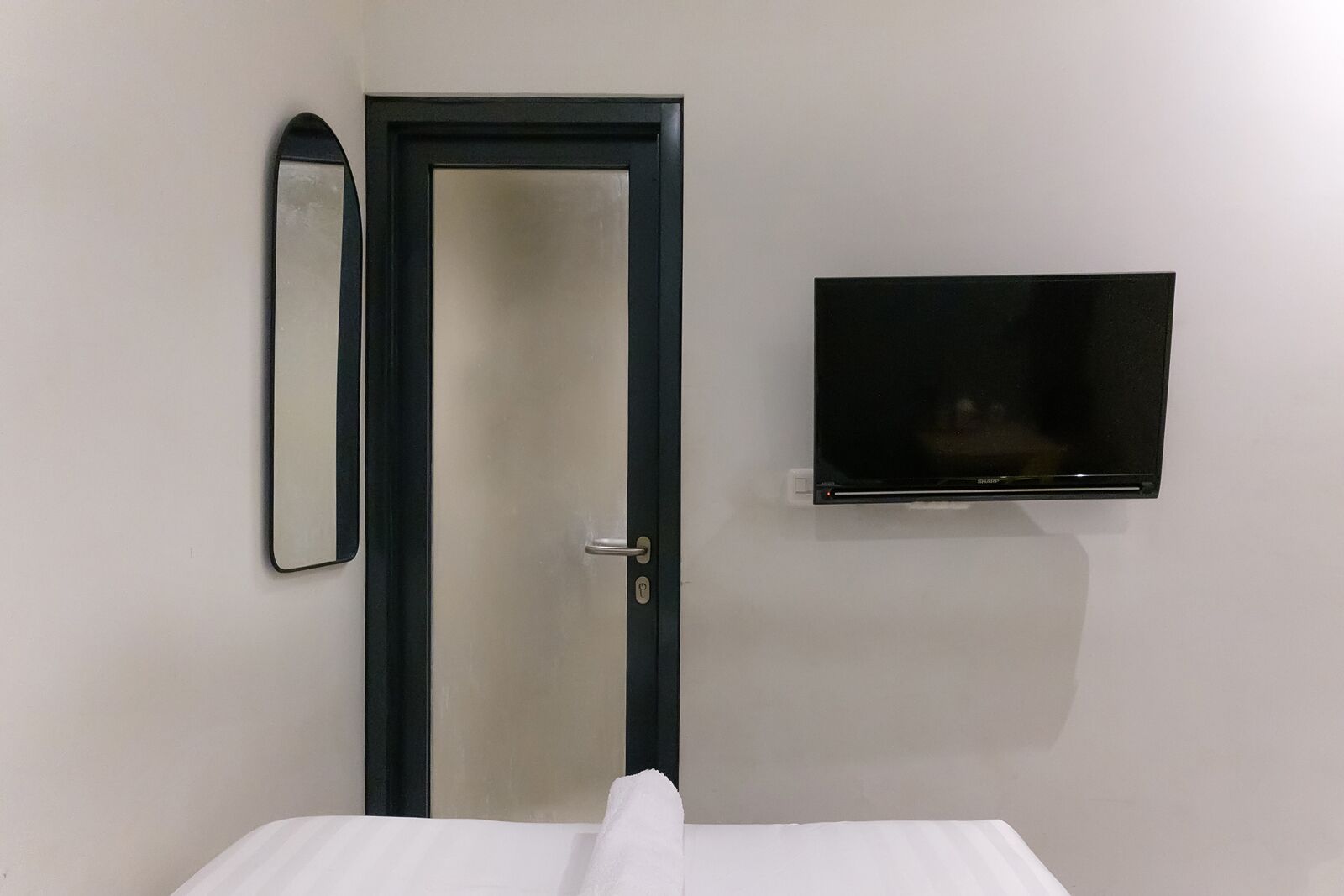 Um quarto com uma cama, uma porta, uma televisão e um espelho.