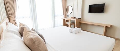 Quarto de hotel com cama, escrivaninha, cadeira, televisão e janela com cortinas.