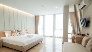 Quarto de hotel moderno com uma cama grande, um sofá, uma TV e uma escrivaninha.