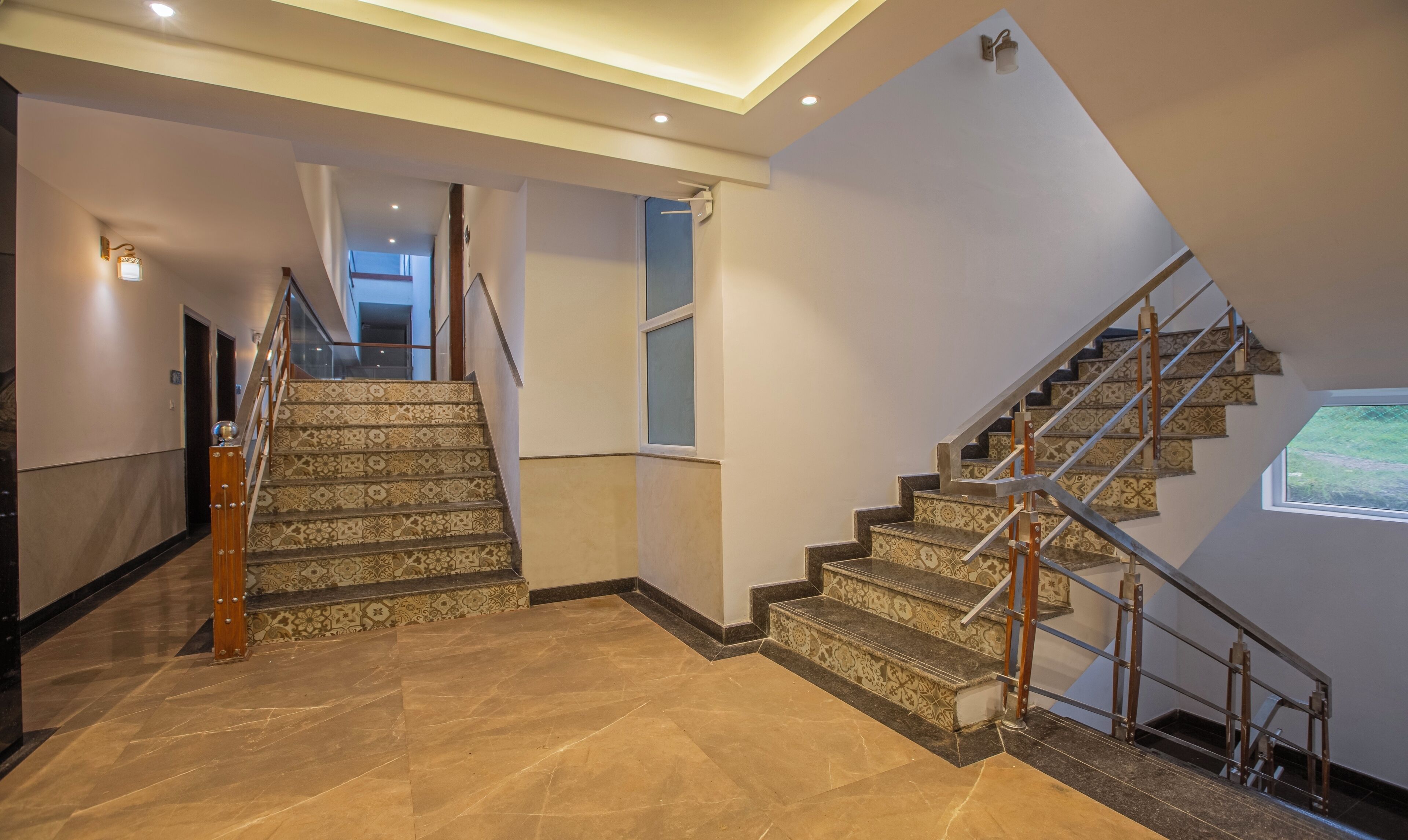 Uma escadaria com degraus estampados e um corrimão de metal, que leva a um patamar com uma porta de vidro.