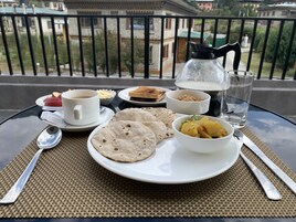 Uma mesa com uma refeição que inclui pão sírio, uma tigela de prato de batatas, uma xícara de café e um copo de água, com vista para edifícios ao fundo.