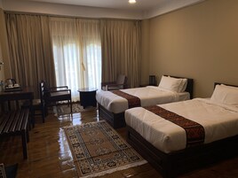 Quarto de hotel com duas camas, uma escrivaninha, uma cadeira e uma pequena mesa com chaleira e chávenas.
