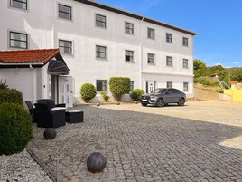Um edifício branco com telhado em telhas, entrada com calçada e um carro estacionado.