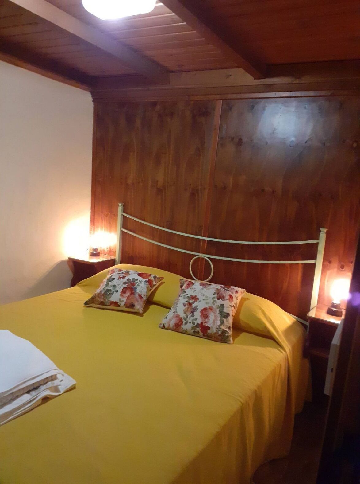 Uma cama de solteiro com almofadas florais, cabeceira de madeira e luminárias de cabeceira.