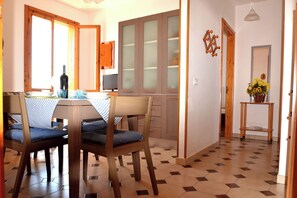 Uma área de refeições com mesa, cadeiras e televisão. Há um armário com portas de vidro jateado e uma porta de madeira com um número.