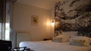 Quarto com cama, poltrona, radiador, parede com mural tropical e um quadro na parede.