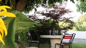 Uma área de estar ao ar livre com uma mesa e duas cadeiras, cercada por vegetação e um poste de luz.