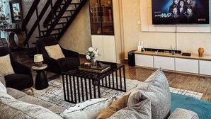Uma sala de estar moderna com escada preta, uma televisão grande e uma área de estar aconchegante.