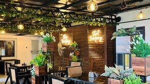 Um restaurante moderno com pé-direito alto, plantas pendentes e mobiliário de madeira.