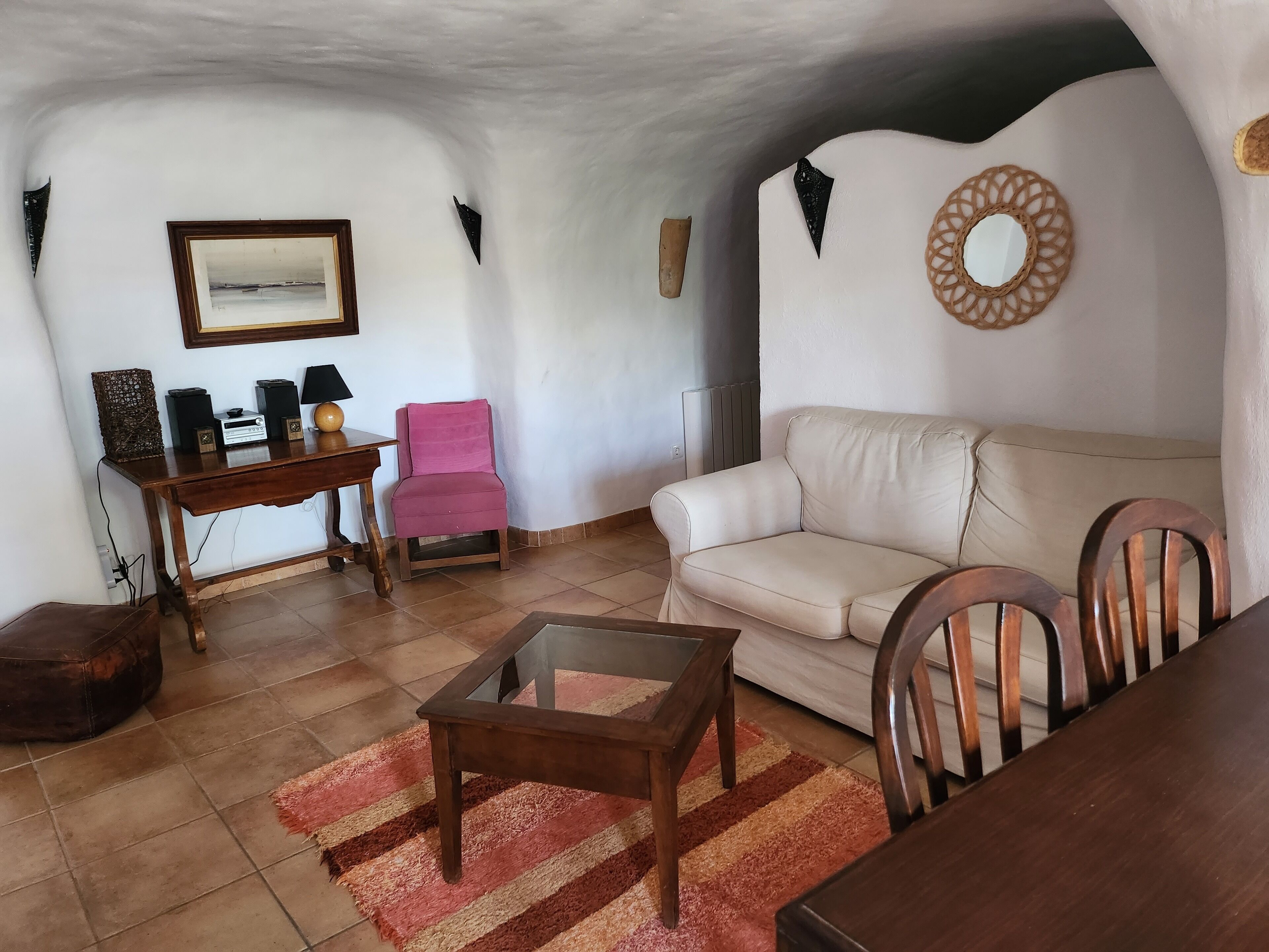 Uma sala de estar com uma mesa de centro de madeira, uma cadeira rosa, um sofá bege e uma mesa de jantar com cadeiras.