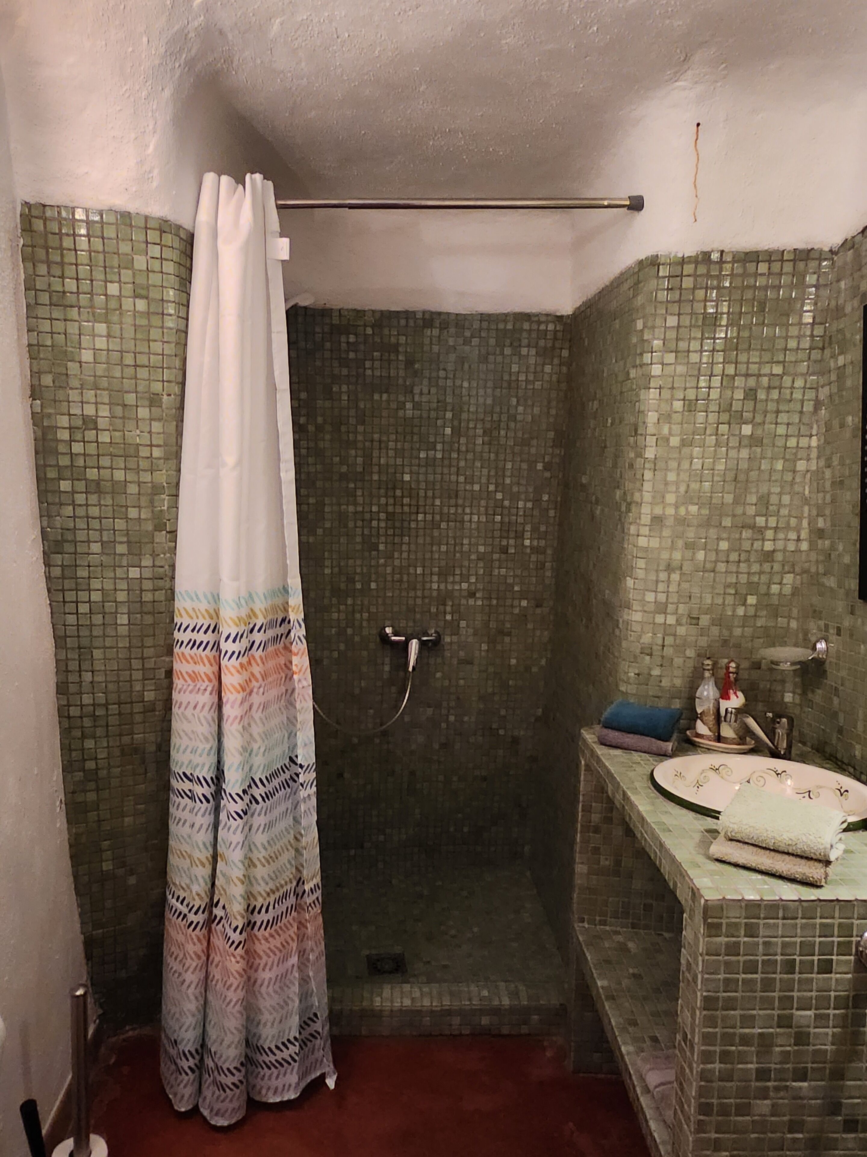 Casa de banho com chuveiro, paredes em azulejo, lavatório com espelho e um porta-toalhas.