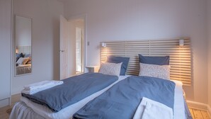 Quarto com cama grande, mesa de cabeceira, espelho e janela com persianas.
